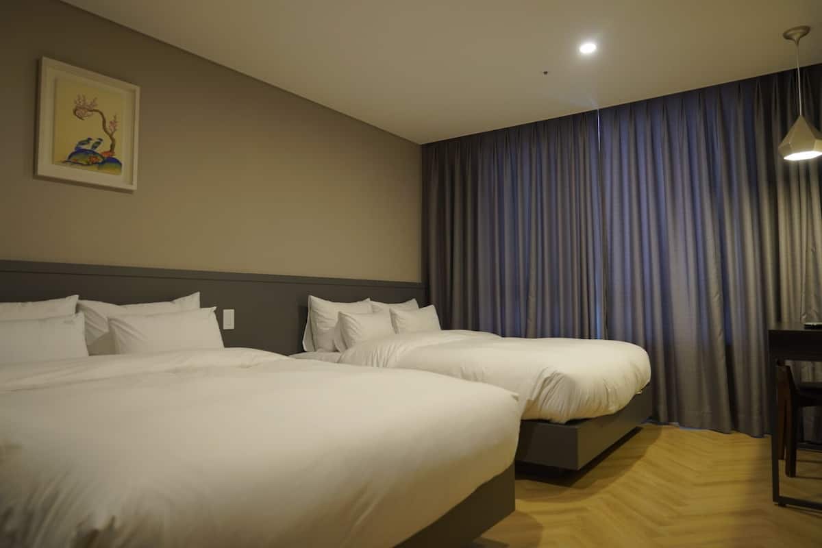 Quarto de hotel com duas camas, um quadro na parede e uma janela grande com cortinas.