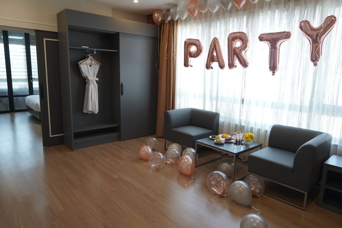 Uma sala de estar moderna com um sofá, uma mesa de centro com petiscos e balões formando a palavra 'PARTY'.