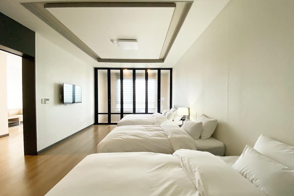 Quarto de hotel moderno com uma cama grande, uma televisão fixada na parede e uma porta de vidro deslizante para uma varanda.
