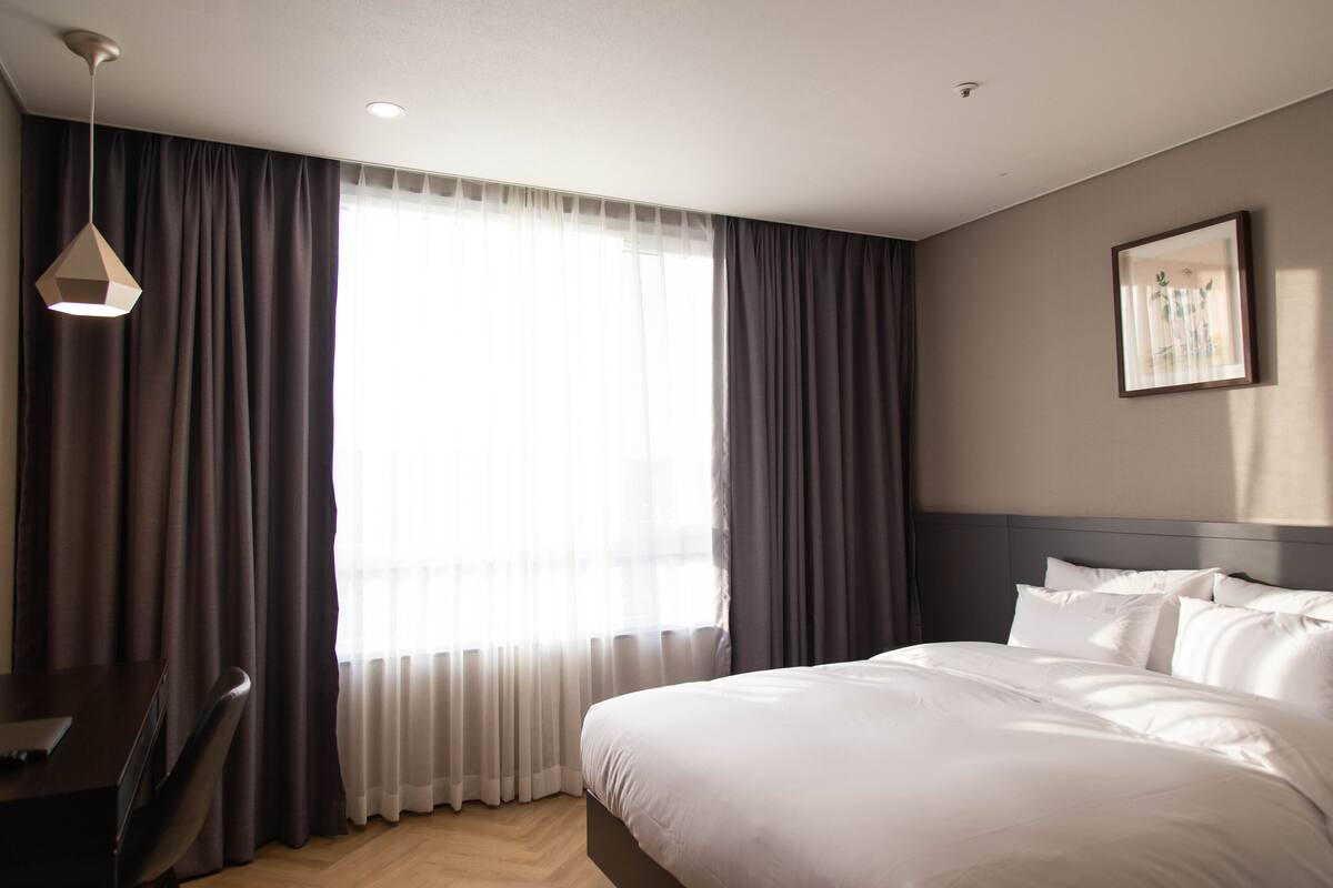 Quarto de hotel com uma cama grande, uma escrivaninha e uma janela com cortinas.