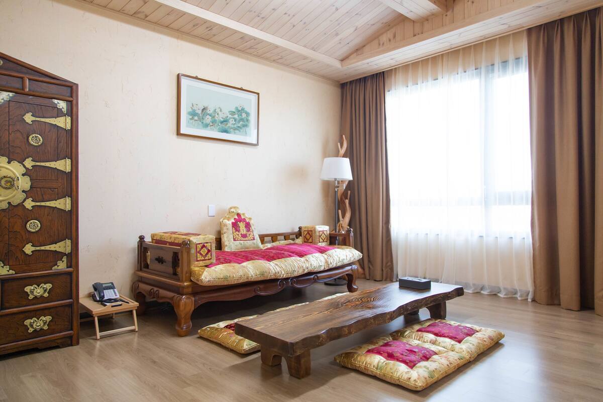 Quarto com cama de madeira, uma mesa, abajur e um quadro na parede.