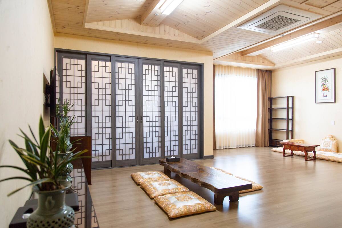 Um quarto tradicional japonês com tatames, uma mesa de madeira baixa, almofadas e uma porta deslizante com padrões geométricos.