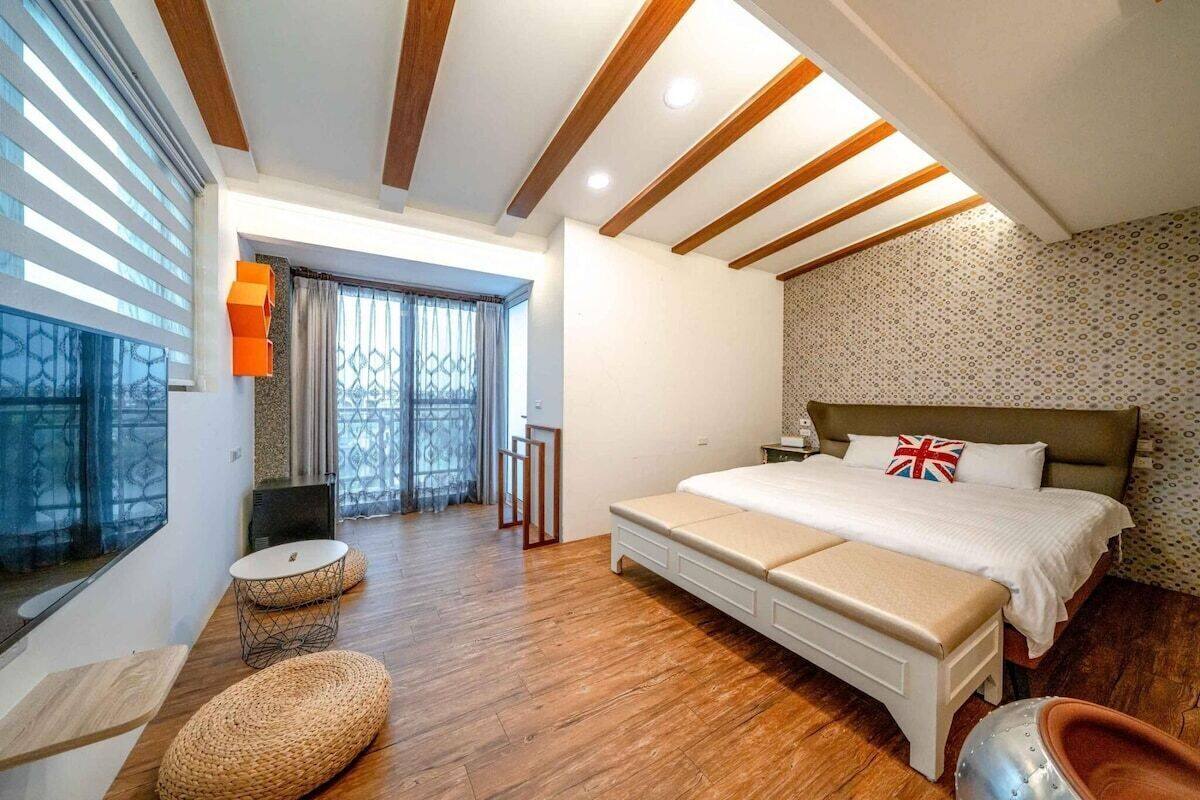 Quarto moderno com uma cama grande, piso de madeira e vista pela janela com persianas.