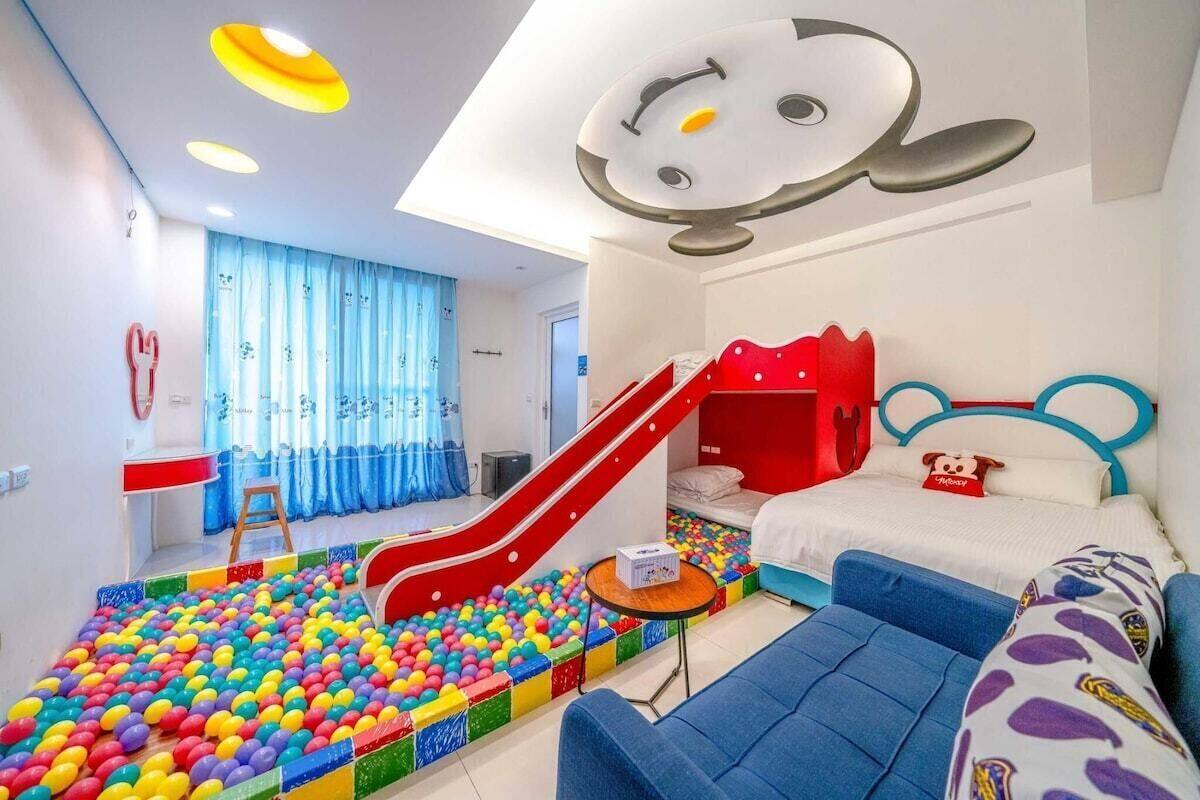 Espaço infantil com escorrega, piscina de bolinhas coloridas e uma cama com tema da Hello Kitty.
