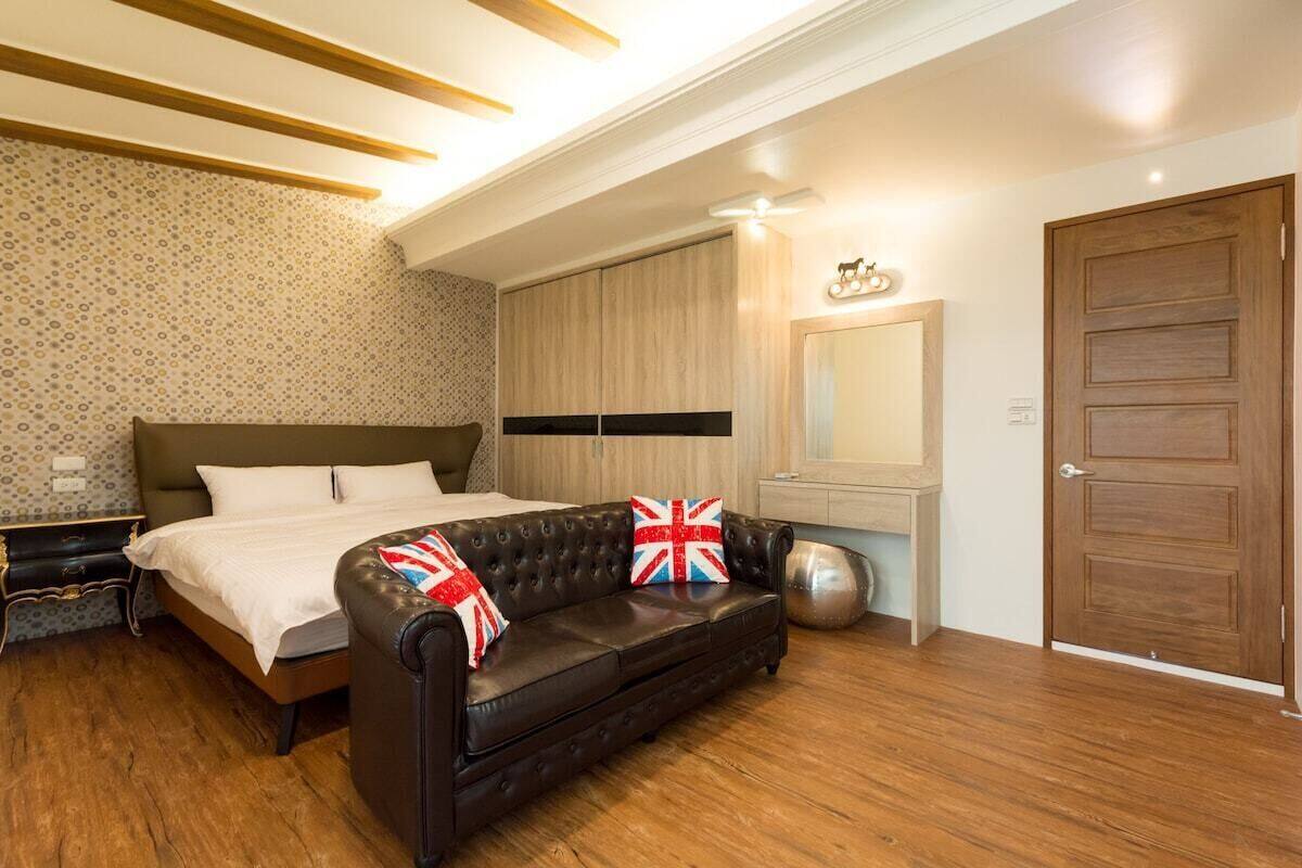 Quarto com cama, sofá de couro com almofadas, guarda-roupa, espelho e porta de madeira.