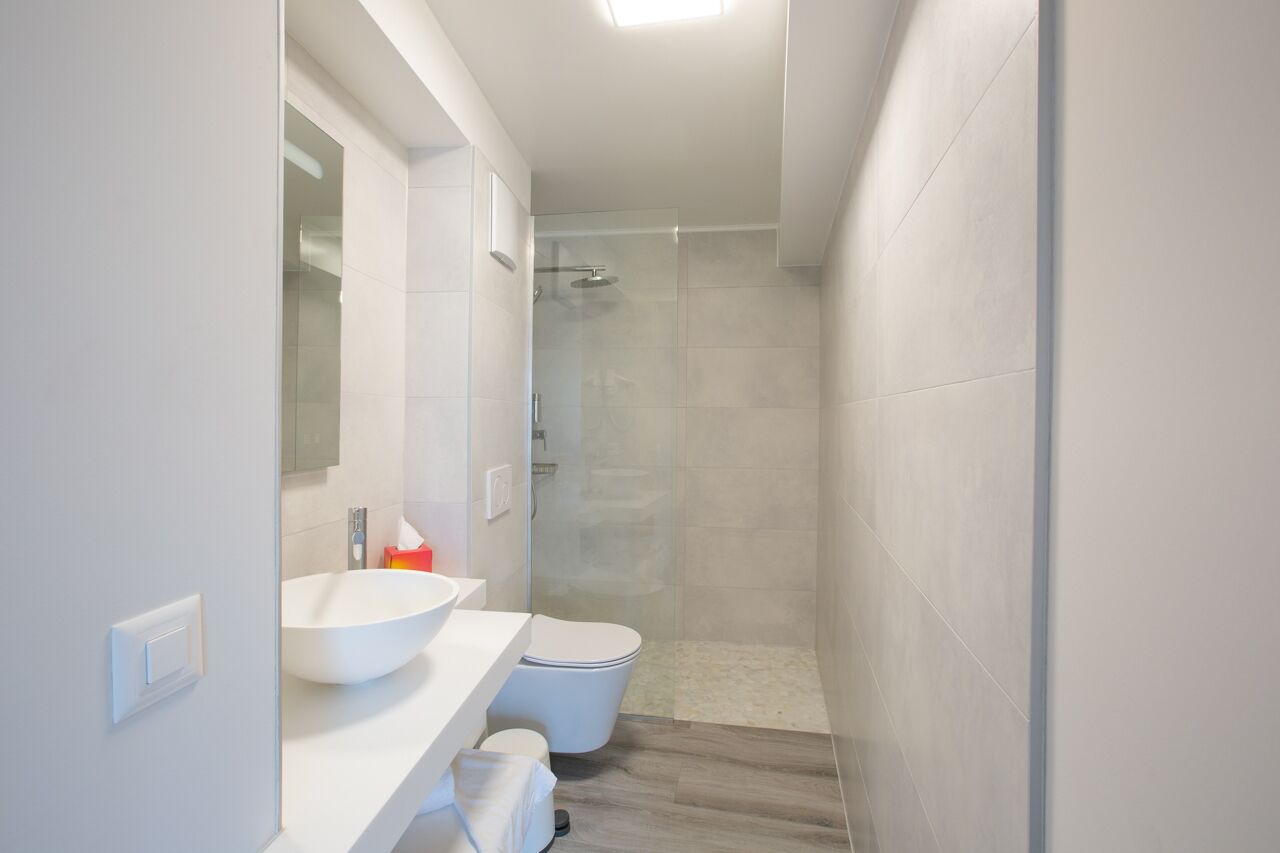 Uma casa de banho moderna com lavatório, sanita e chuveiro, tudo em branco.