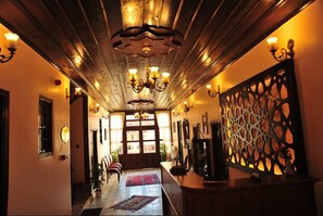 Corredor com vigas de madeira, um candelabro e um painel decorativo.