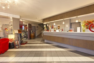 Uma área de recepção de hotel com design moderno, balcão de recepção, escada e um espaço de estar com uma cadeira vermelha.
