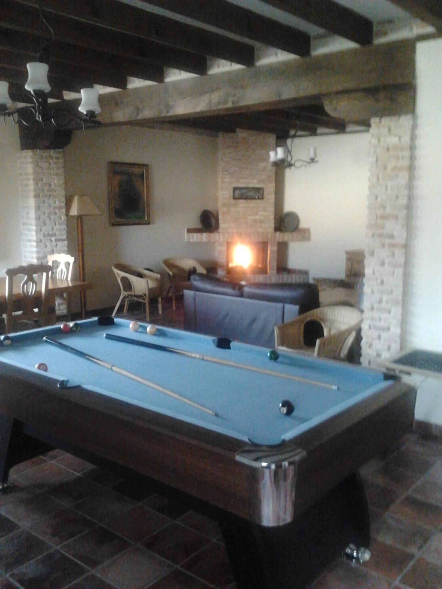 Uma mesa de bilhar em um espaço com vigas aparentes, lareira e parede de pedra.