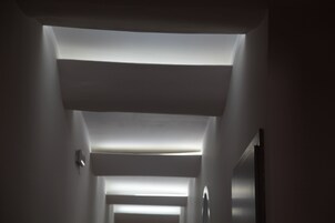 Um corredor estreito e pouco iluminado, com teto inclinado e iluminação embutida.