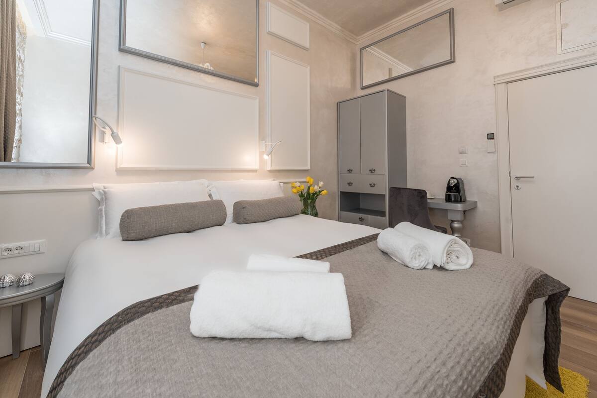 Quarto de hotel moderno com uma cama grande, mesas de cabeceira, espelho e guarda-roupa.