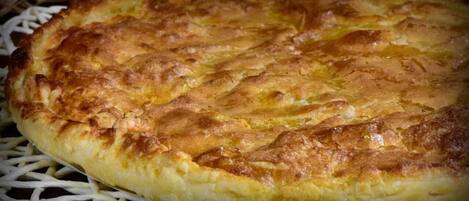 Um prato grande, redondo e dourado assado, possivelmente uma torta salgada, sobre uma camada de material branco desfiado, provavelmente queijo ou legumes.