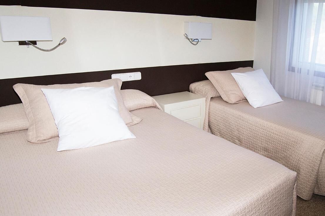 Quarto de hotel com duas camas de solteiro, cada uma com almofada e mesa de cabeceira.