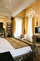 Um quarto espaçoso com uma cama grande, um candelabro, uma lareira e uma televisão.