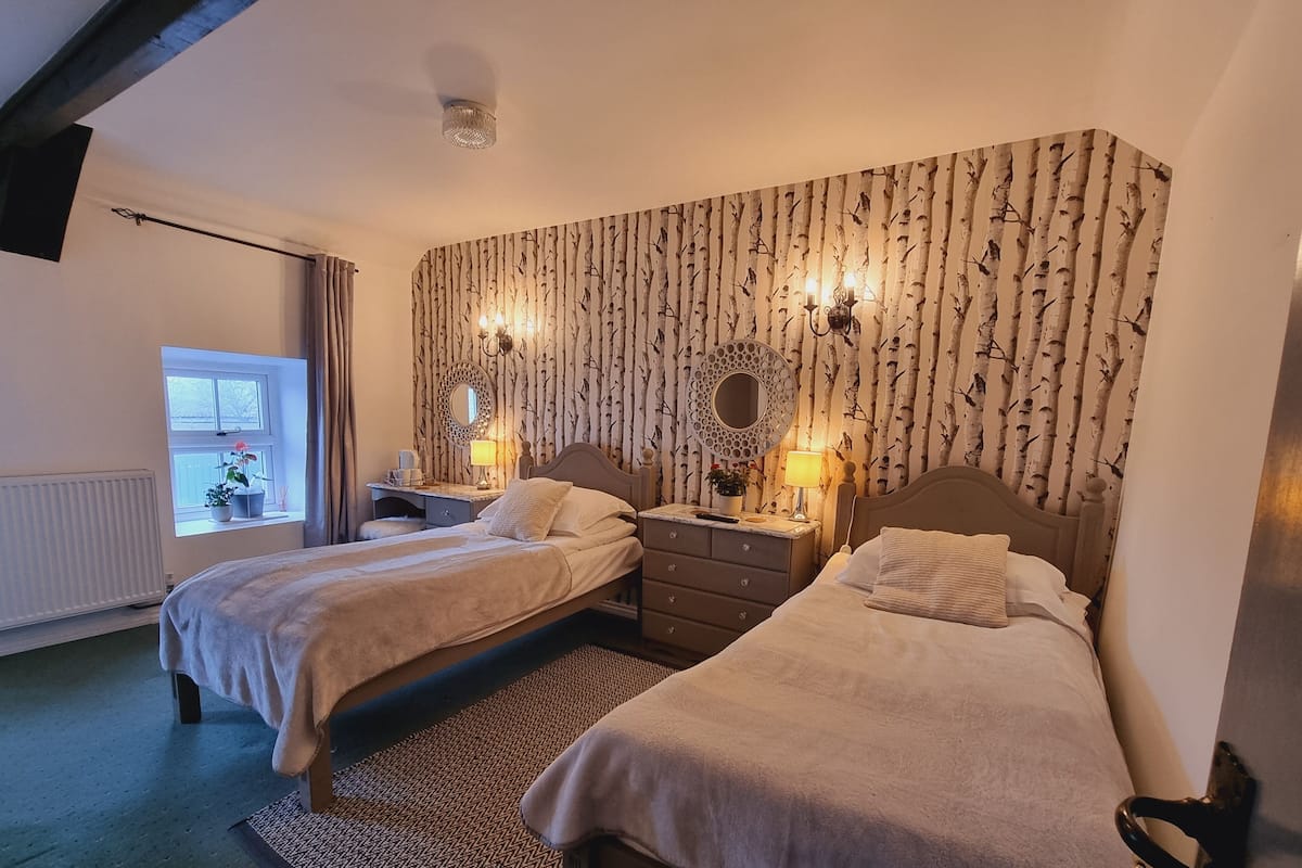 Quarto duplo com duas camas, penteadeira, espelho e janela com cortinas.