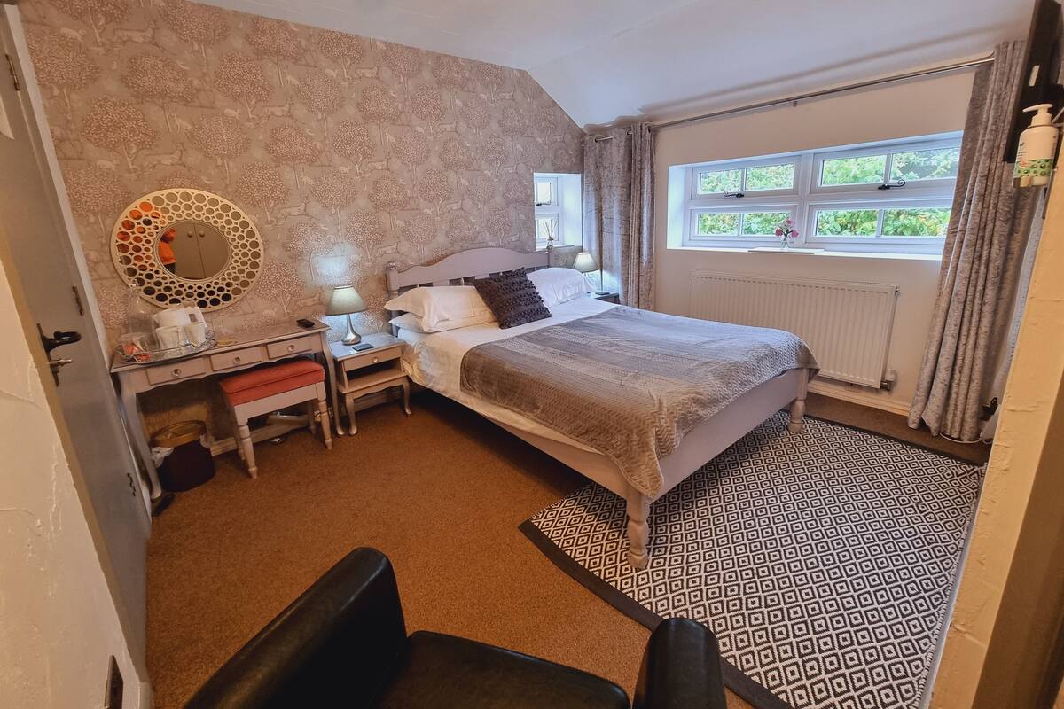 Quarto com cama, mesas de cabeceira, espelho, janela com cortinas e tapete estampado.