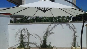 Um guarda-sol branco com estrutura preta, uma parede branca e duas plantas em vasos com trepadeiras.