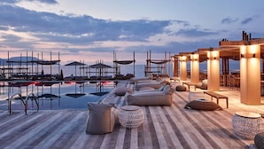 Uma área de lounge no terraço com espreguiçadeiras, piscina e uma pérgola de madeira com iluminação.