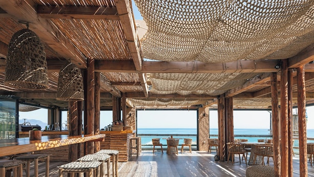 Uma área de bar com móveis de vime e vista para o mar.