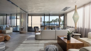 Uma sala de estar moderna com sofá modular, uma mesa de centro de madeira e vista para o oceano através de grandes janelas.