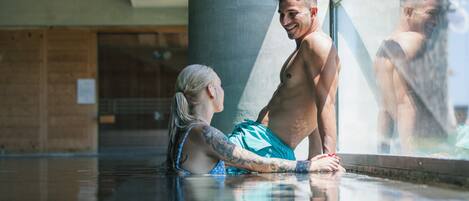 Um homem e uma mulher em uma piscina, com uma grande janela de vidro refletindo a imagem deles.