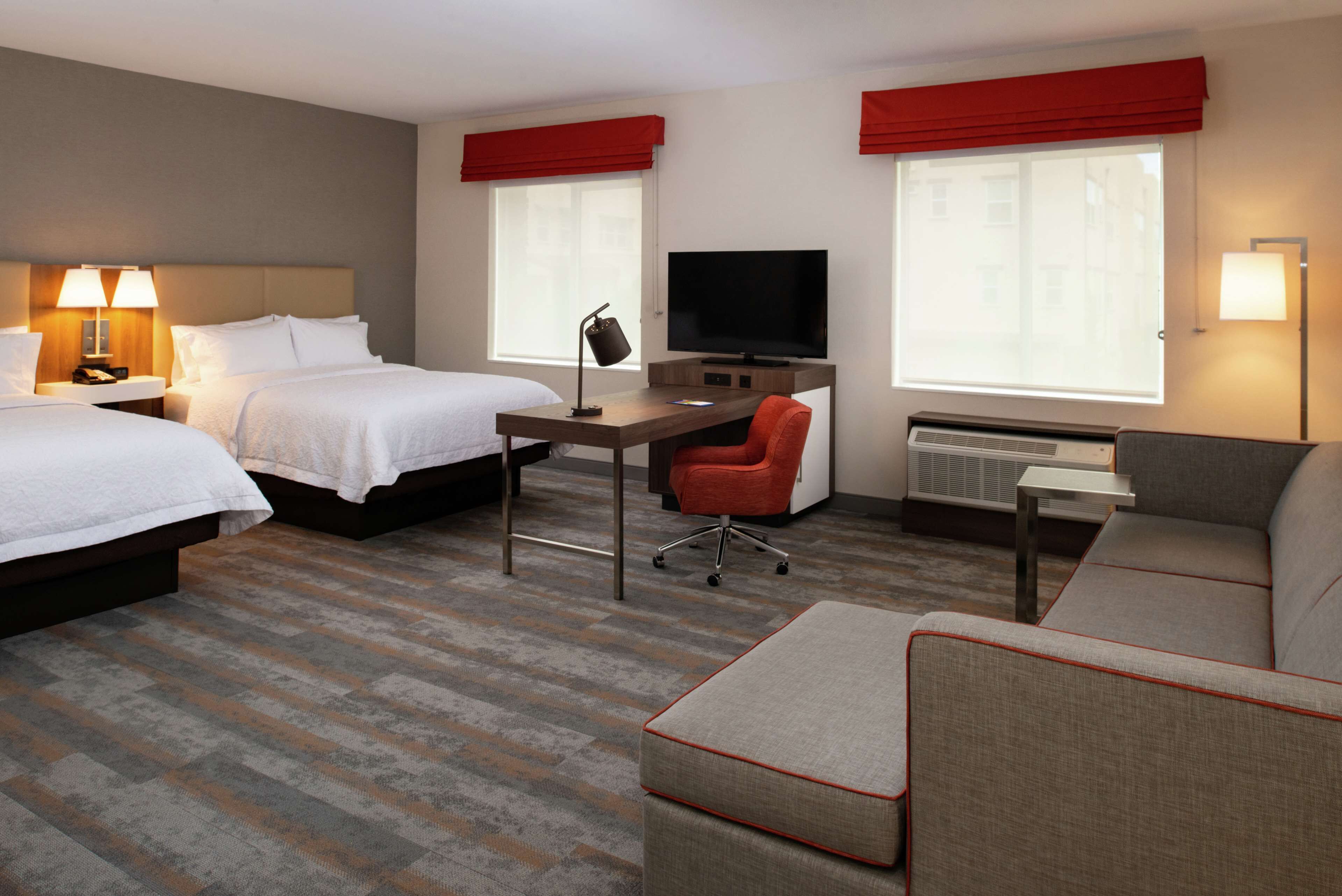 Quarto de hotel com duas camas, uma mesa de escritório com cadeira, televisão e um sofá.
