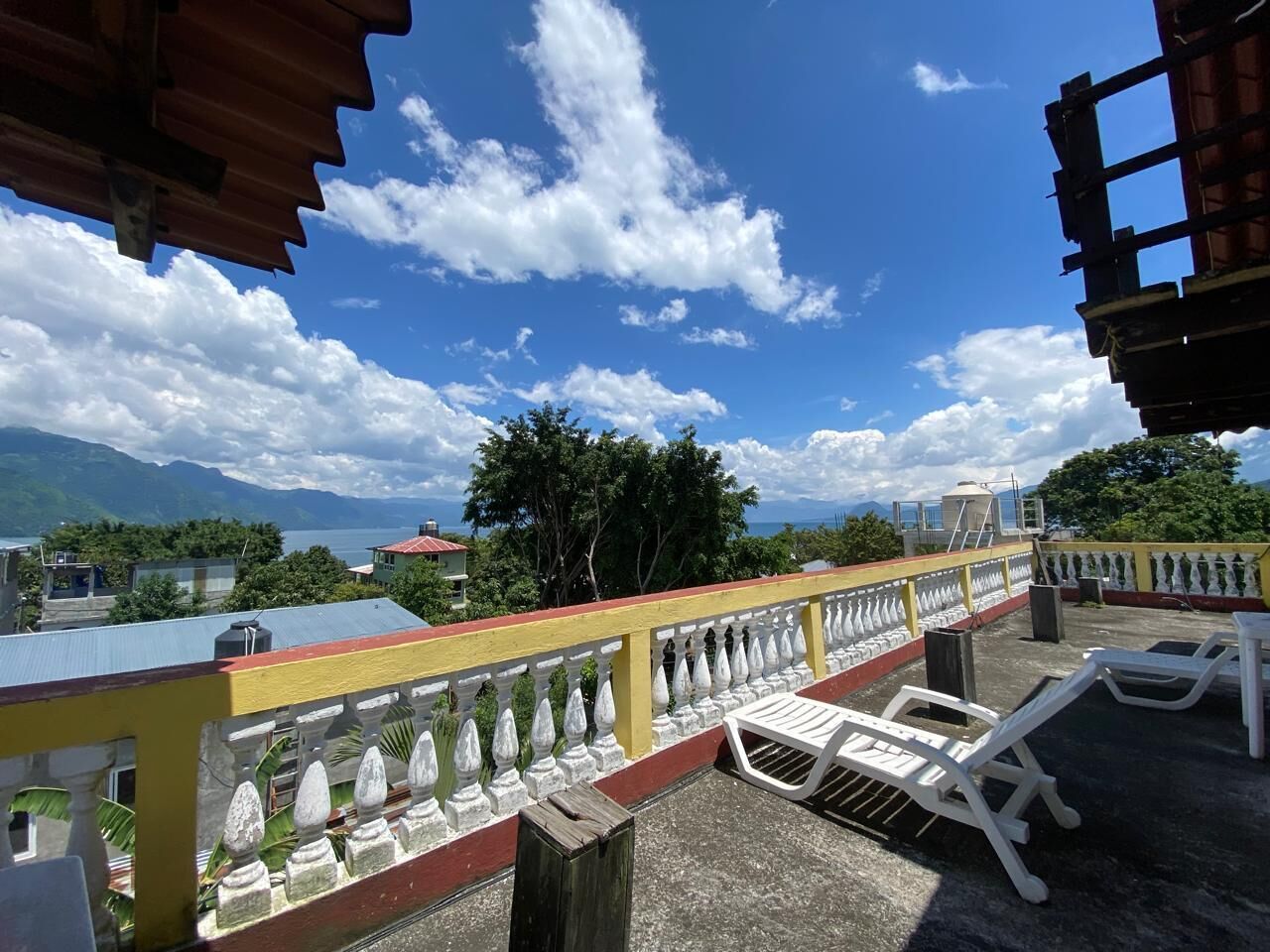 Terraço no telhado com guarda-corpo amarelo, cadeiras de descanso brancas e vista para montanhas e um corpo d'água.