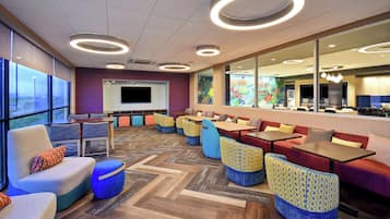 Um restaurante moderno com diversas opções de assento, incluindo cabines, mesas e banquetas altas. Há uma grande janela que oferece vista para a paisagem urbana, e o interior combina piso de madeira e carpete.