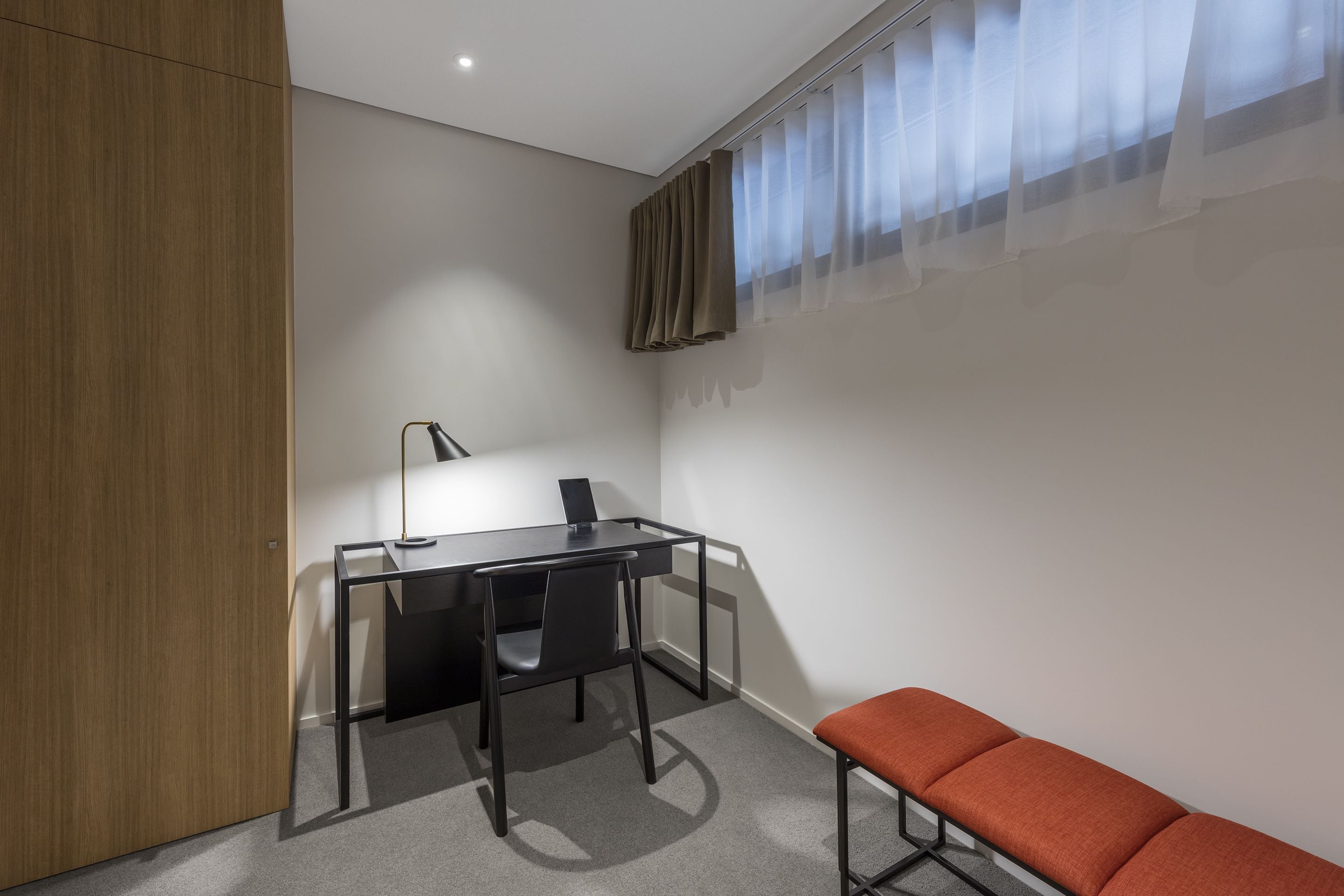 Quarto pequeno e moderno com escrivaninha, cadeira e um banco.