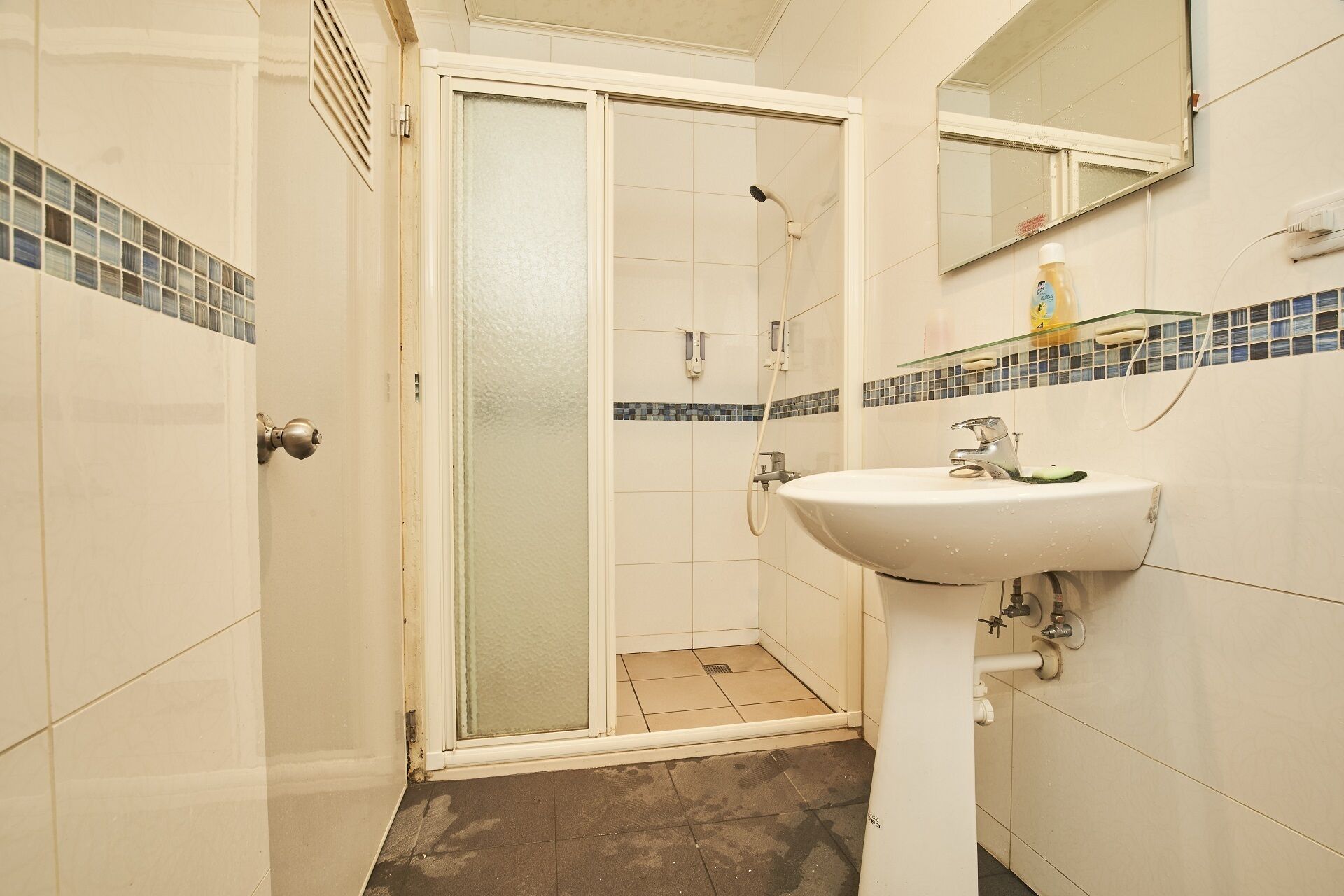 Um banheiro com chuveiro de porta de vidro, pia com espelho acima e piso de azulejos.