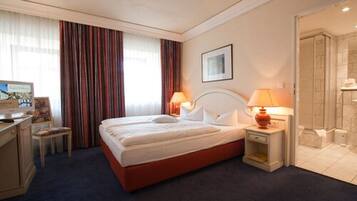 Quarto de hotel com cama, duas mesas de cabeceira, escrivaninha, cadeira, chuveiro e cortinas.