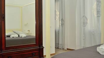 Quarto com um espelho grande, uma cama com colcha cinza e cortinas brancas com estampas florais.
