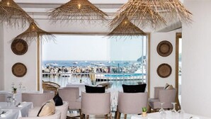 Um restaurante com mesas e cadeiras, vista para barcos e um porto de iates, e pratos decorativos na parede.