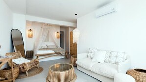 Quarto moderno com cama branca, área de estar com sofá branco e cadeiras de vime, mesa redonda de vime e um espelho grande na parede.