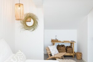 Quarto minimalista com um banco de madeira, cestos de vime e uma pequena mesa de madeira com uma garrafa de água.