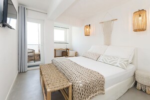Quarto com uma cama grande, um banco, uma televisão e vista para o exterior.