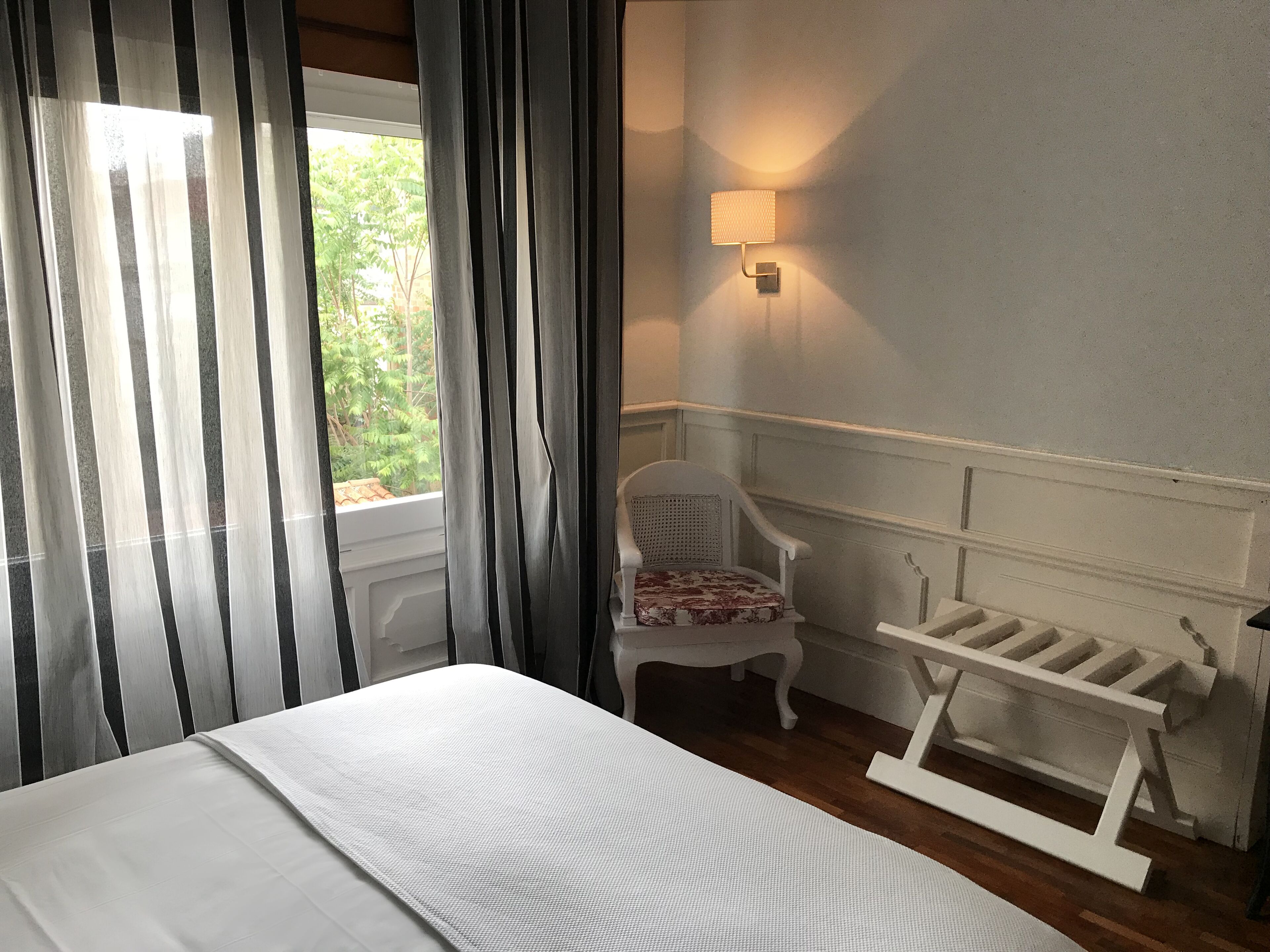 Um quarto com cama, poltrona, mesa de cabeceira e luminária na parede.