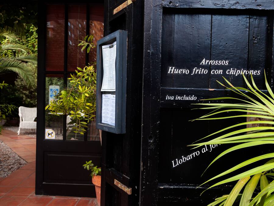 Uma porta de madeira preta com texto indicando um menu de Arrossos, oferecendo batatas fritas com batata palha e uma bebida.