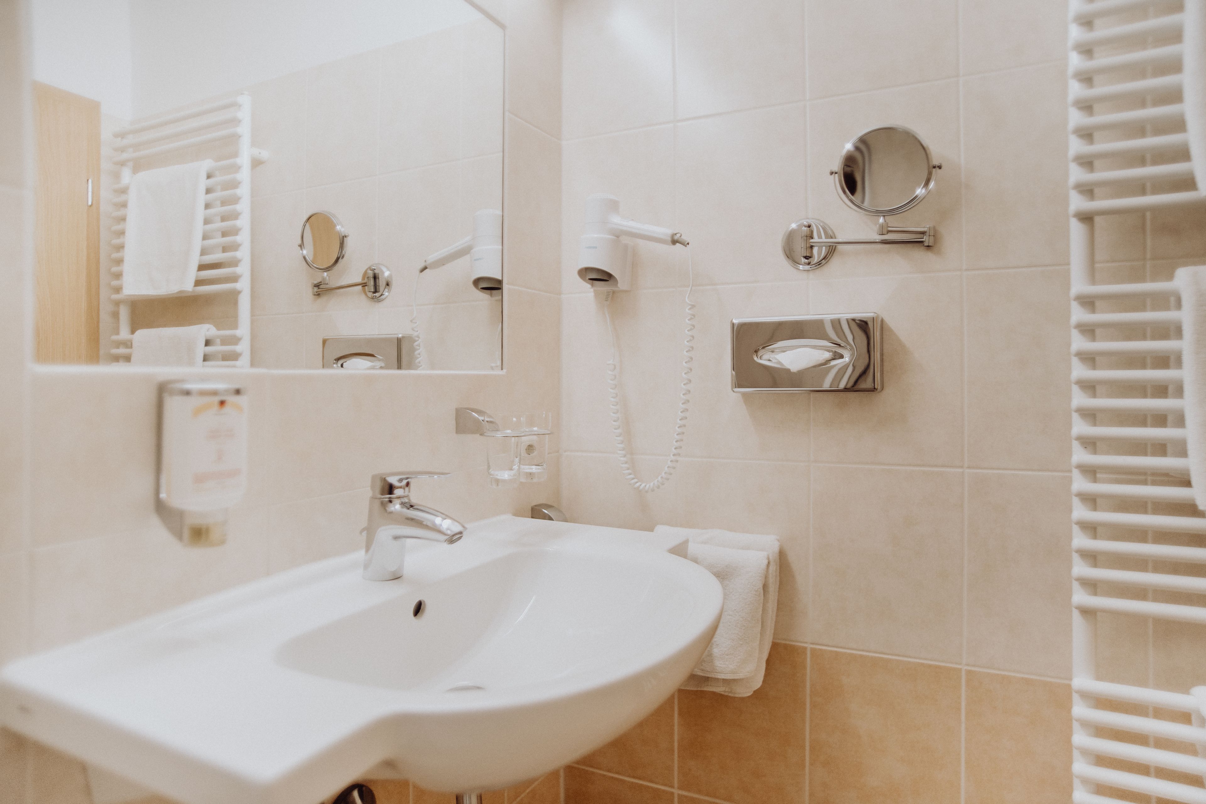 Casa de banho moderna com lavatório branco, porta-toalhas, espelho e secador de cabelo.