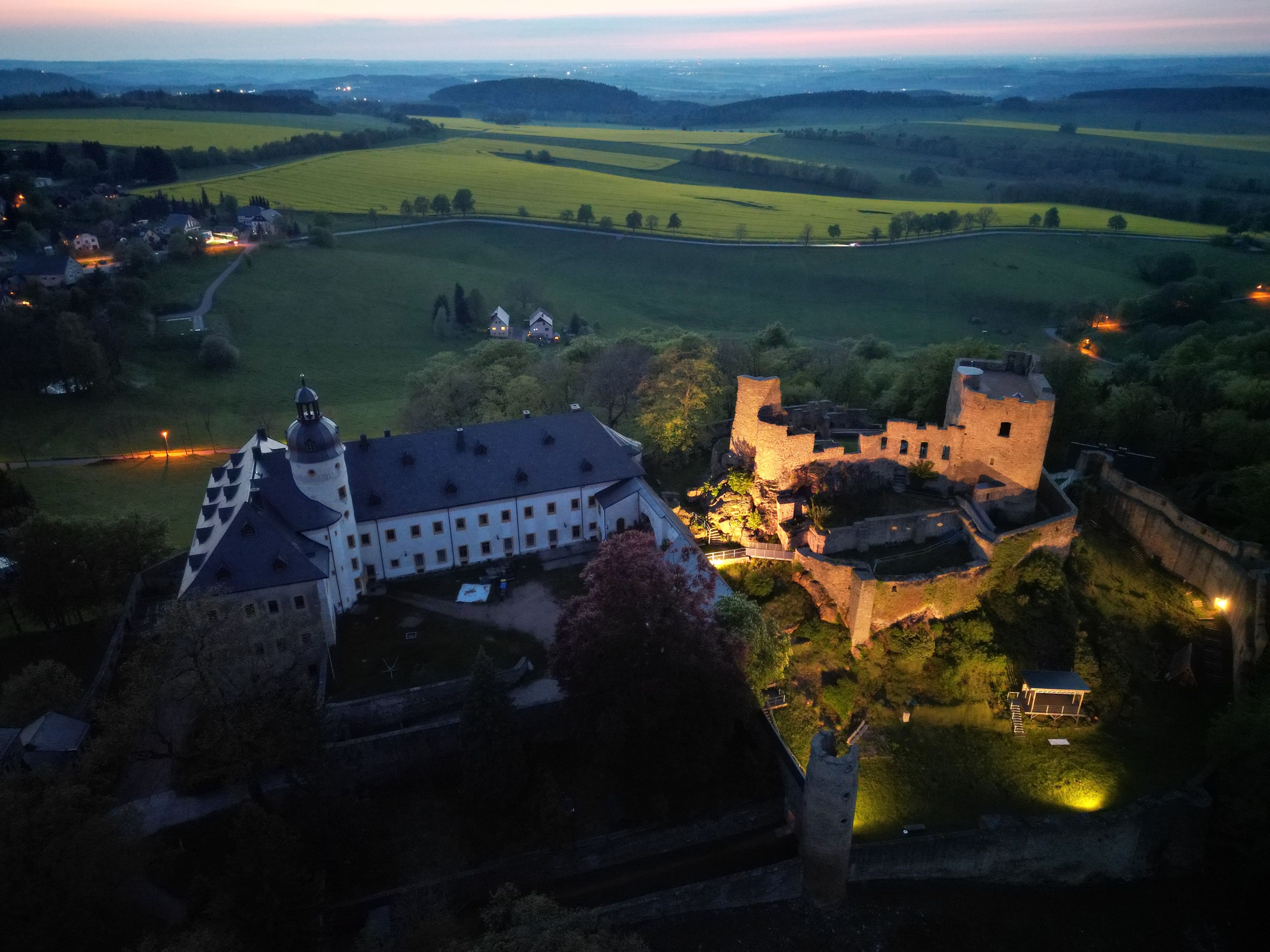 Um castelo com um pátio espaçoso, rodeado por campos e alguns edifícios.
