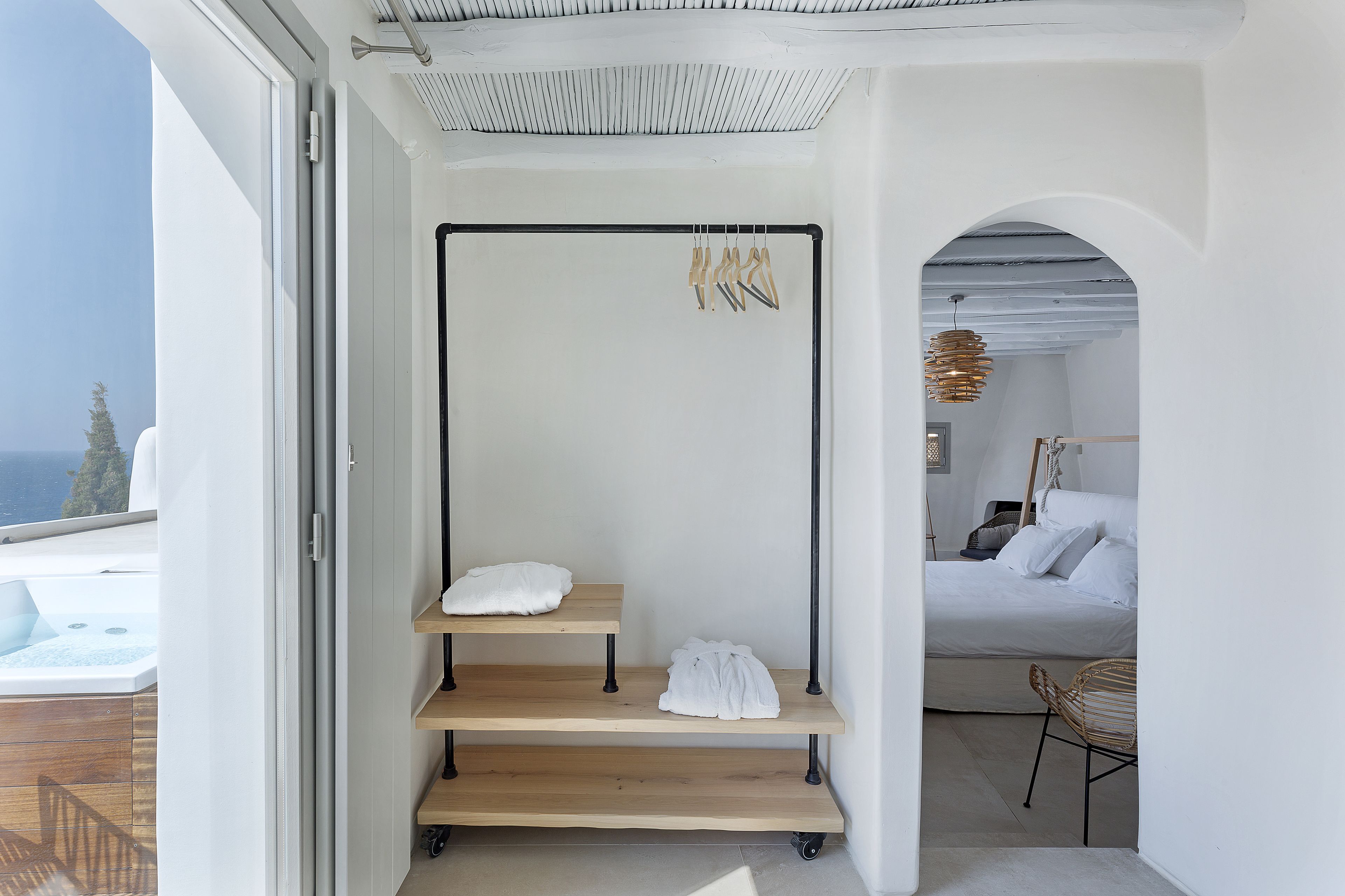 Quarto moderno com cama, estante de madeira e vista para o mar.