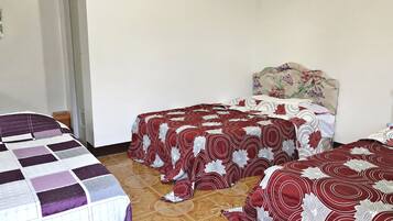 Quarto com duas camas, cada uma com colcha de padrão floral, cabeceira lisa e piso de azulejos.