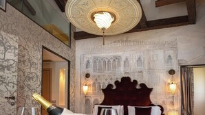 Quarto de hotel luxuoso com uma cama grande, um candelabro e uma mesa posta com taças de champanhe e uma garrafa.