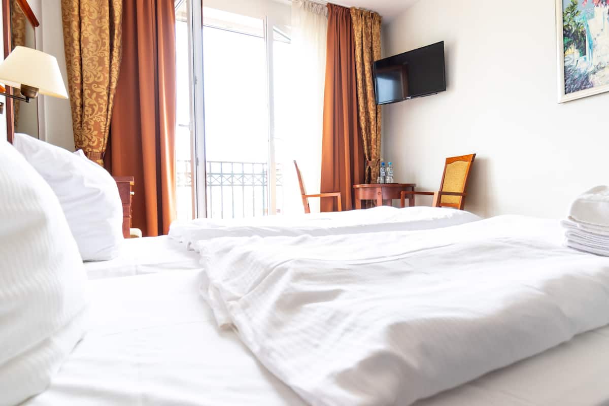 Quarto de hotel com duas camas, uma TV fixada na parede, uma mesa e uma cadeira.
