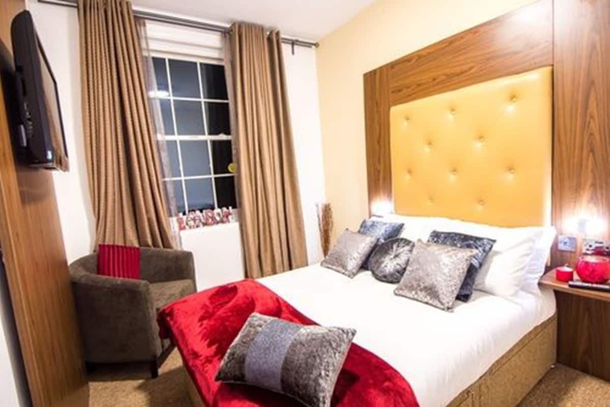 Quarto de hotel com cama, poltrona, televisão e janela com cortinas.