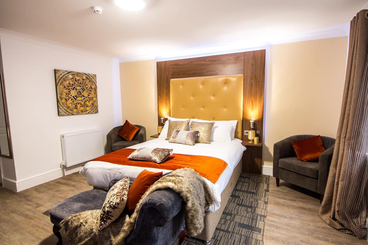 Quarto de hotel com uma cama grande, uma cadeira, um sofá, uma cabeceira de madeira e uma obra de arte na parede.