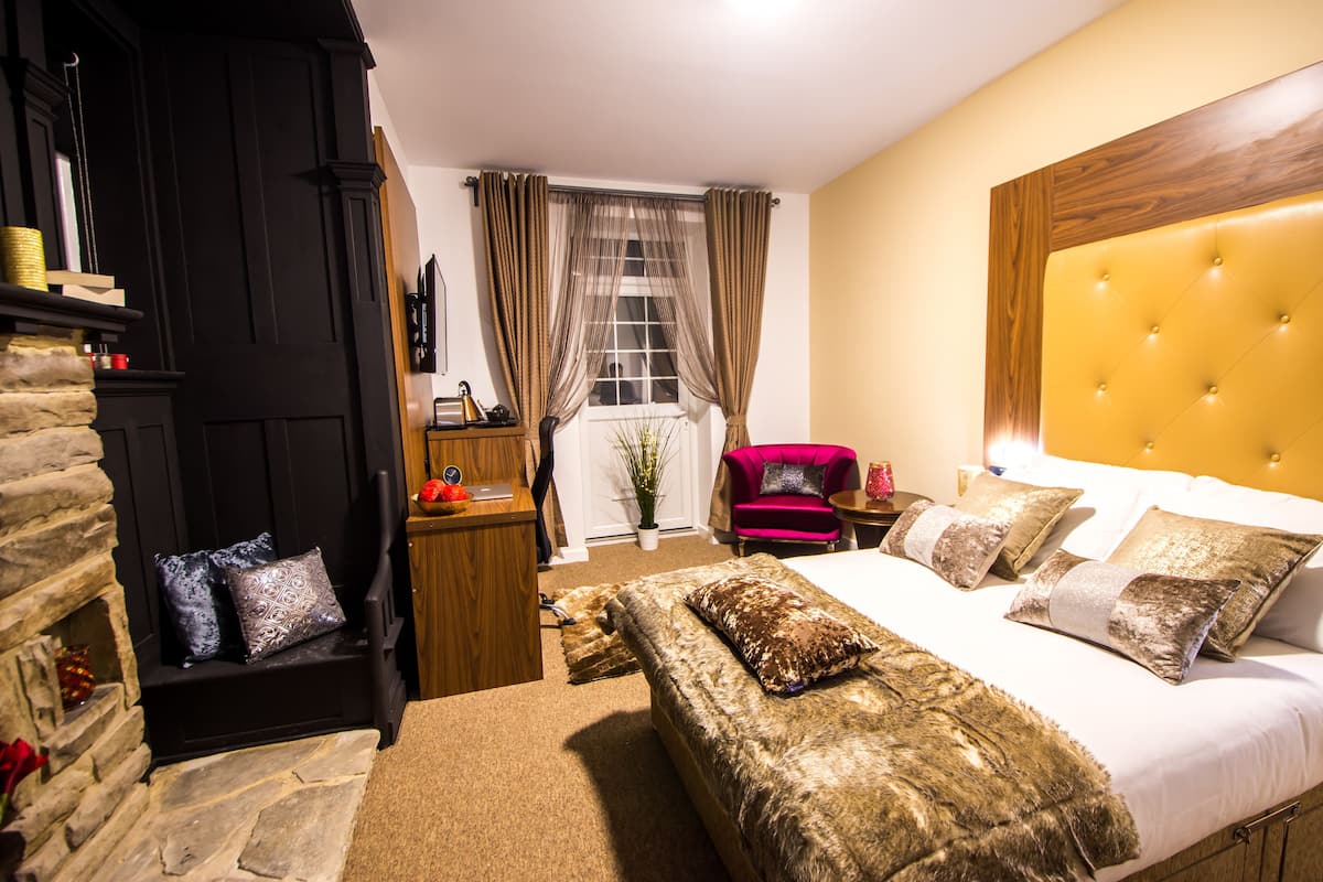 Quarto com uma cama grande, lareira de pedra, cabeceira de madeira e janela com cortinas.