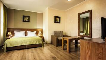 Quarto de hotel com uma cama, mesas de cabeceira, uma cadeira, uma mesinha e um espelho.