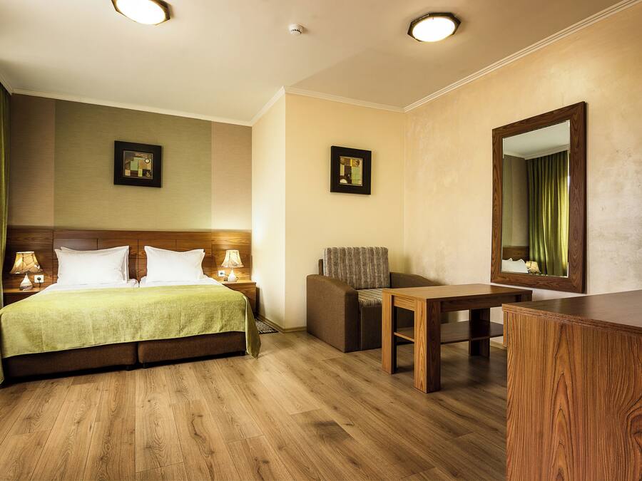 Quarto de hotel com uma cama, mesas de cabeceira, uma cadeira, uma mesinha e um espelho.