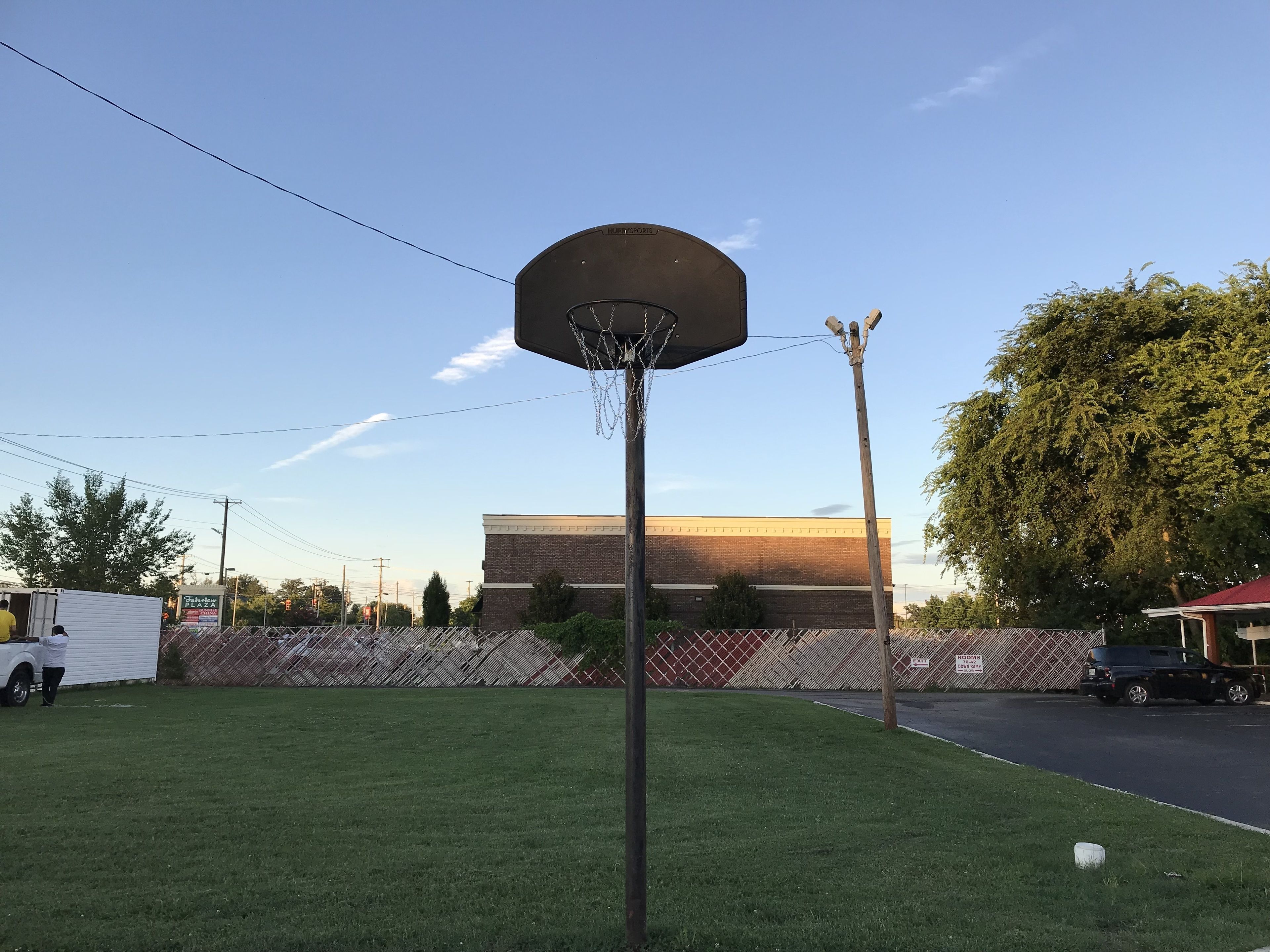 Um cesto de basquete numa área gramada, com um edifício de tijolos ao fundo.
